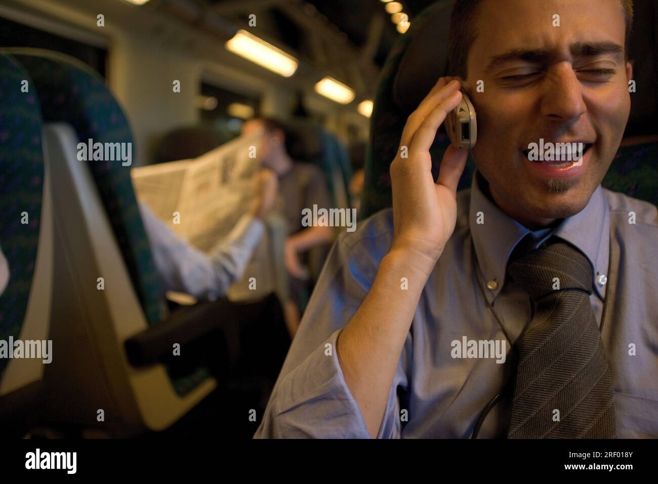 A man talking on the phone in a train compartment, with a passenger ...