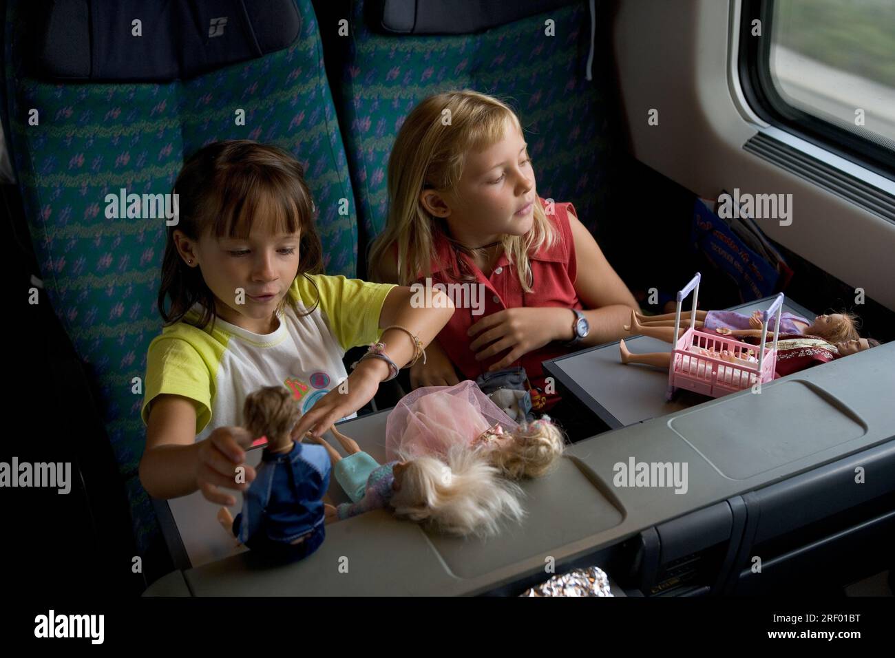 Two children playing with dolls on a train journey in Italy, seated by the window Stock Photo ...