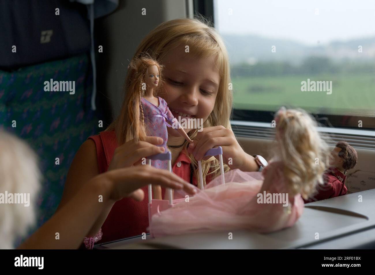 A child playing with dolls on a train journey through the countryside ...