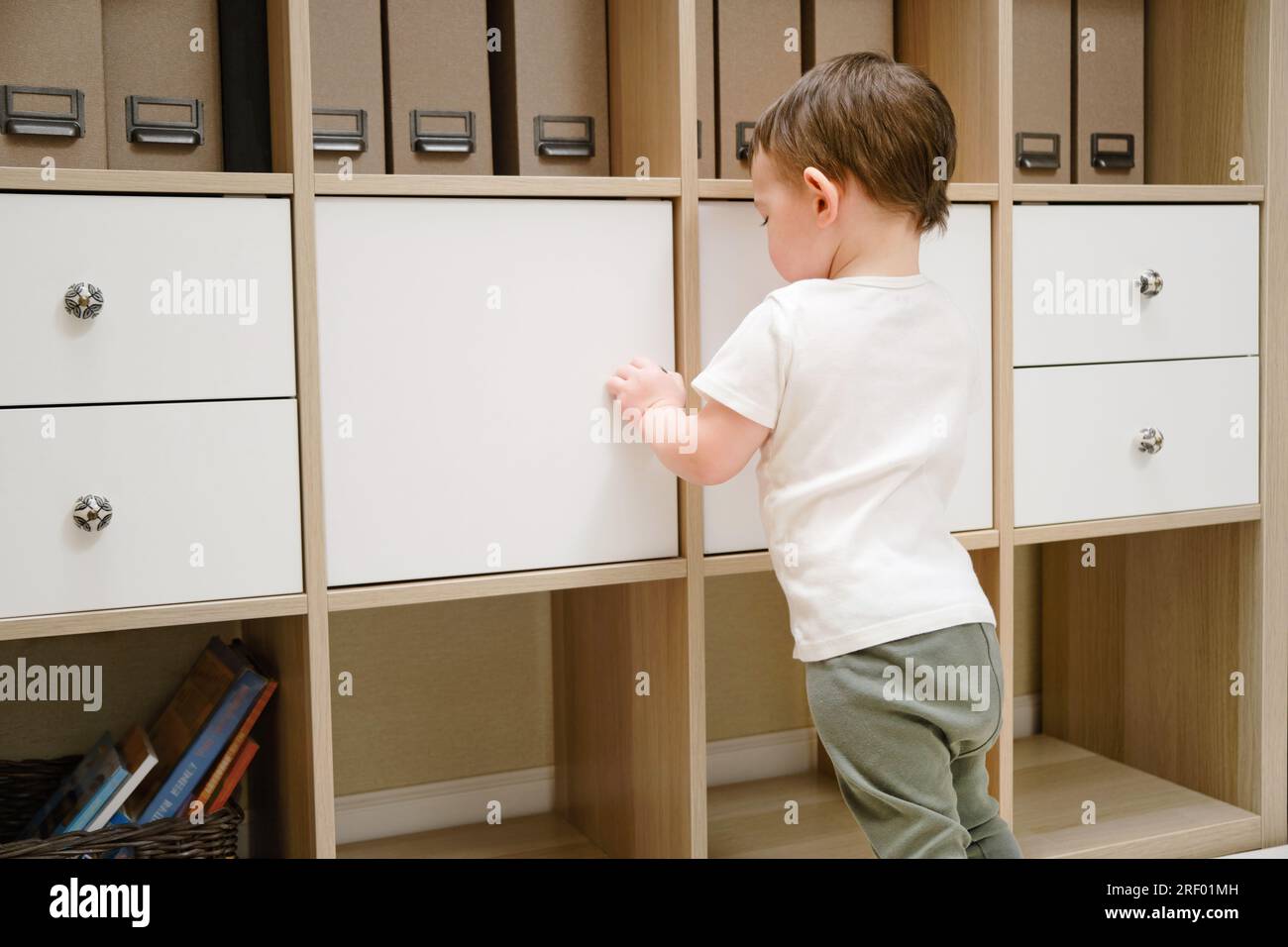 Toddler baby opens the closet door in the home living room. A small ...