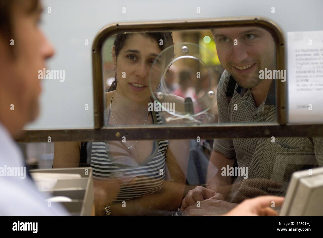 Two people at a ticket counter, viewed through a glass window in Italy ...