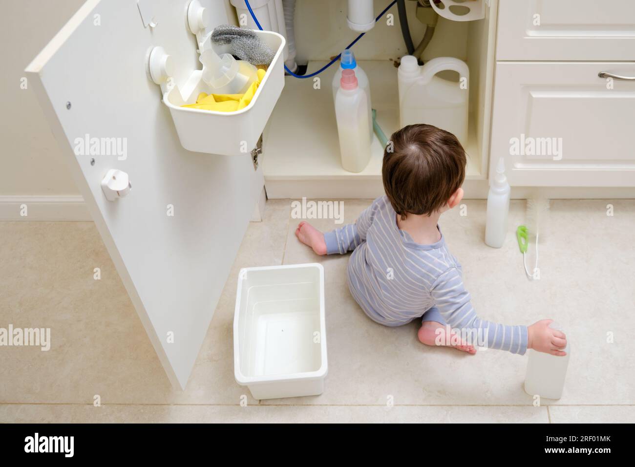 A child is playing with chemical cleaning products under the sink in ...