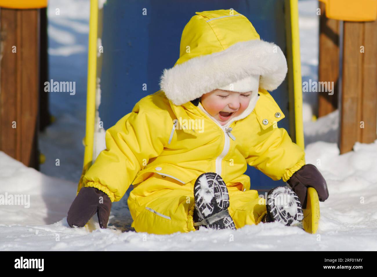 Toddler baby boy rides down a slide playing on a winter playground. A ...