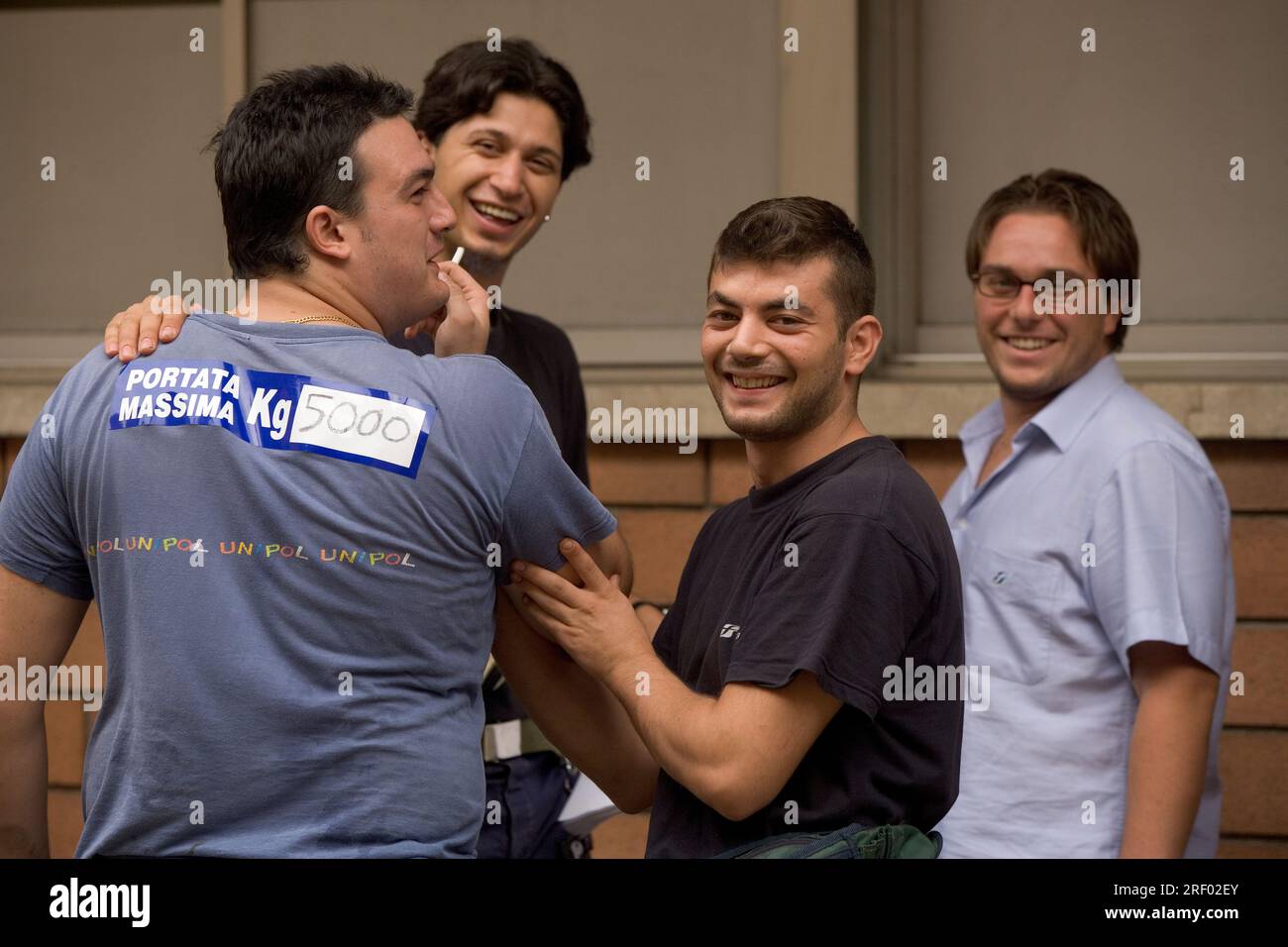 Four men smiling, one wearing a shirt labeled 'PORTATA MASSIMA Kg 5000 ...