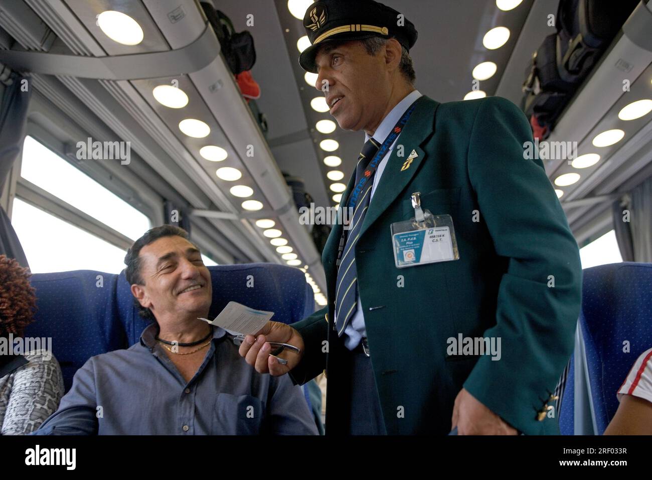 A smiling passenger interacts with a conductor checking tickets on a ...