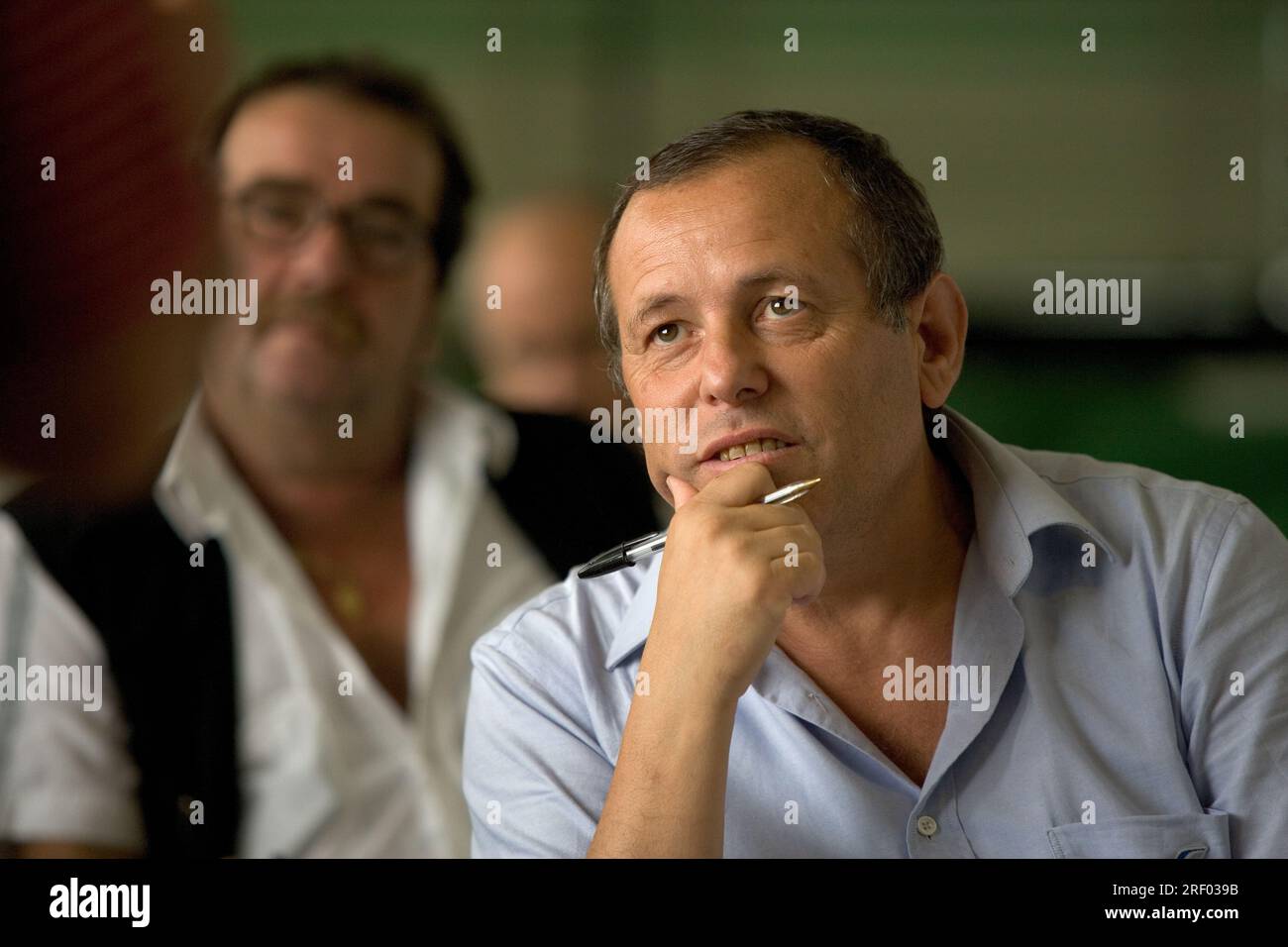 Two men attentively listening during a discussion, one holding a pen ...