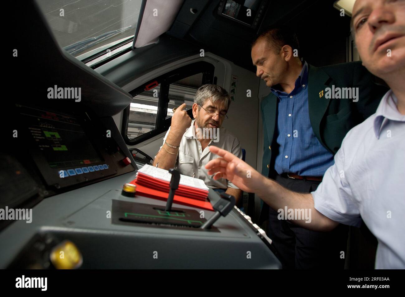 Three men discuss inside a train cockpit, focusing on controls and ...