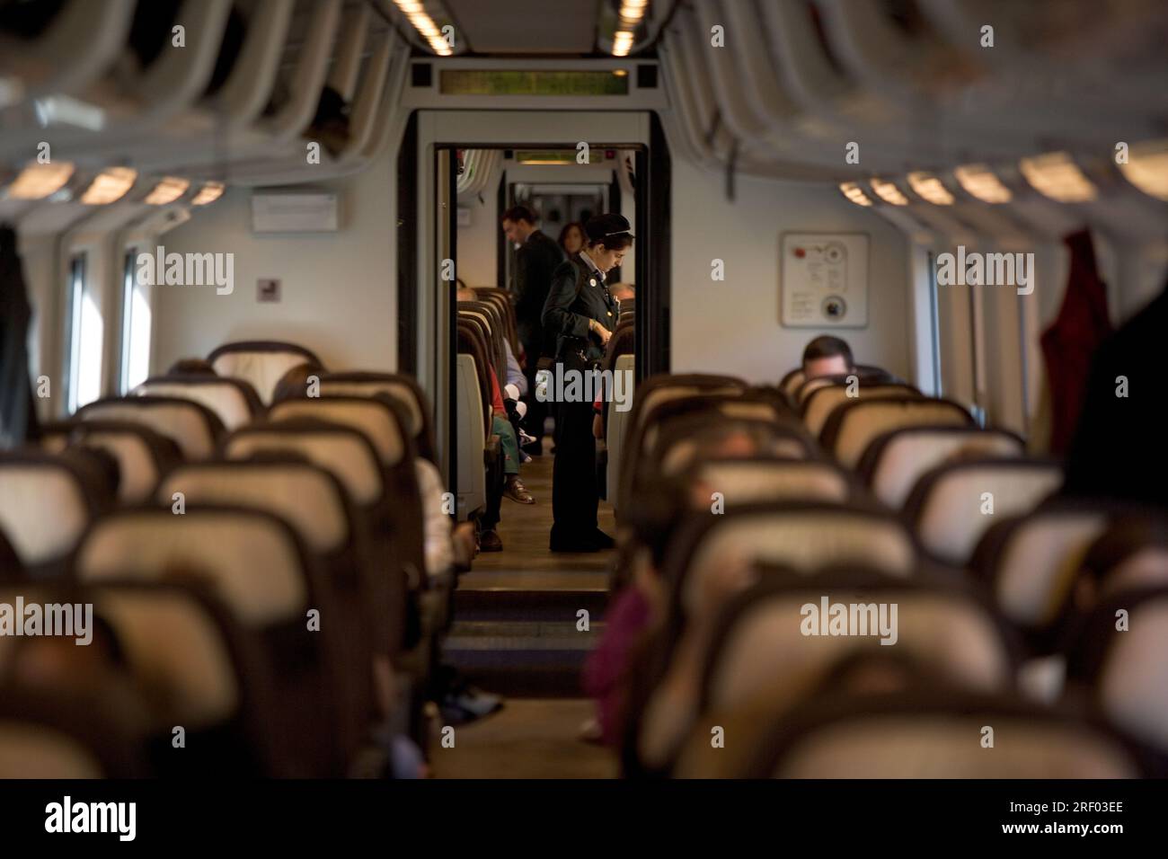 Interior of a train carriage with passengers seated and a conductor ...