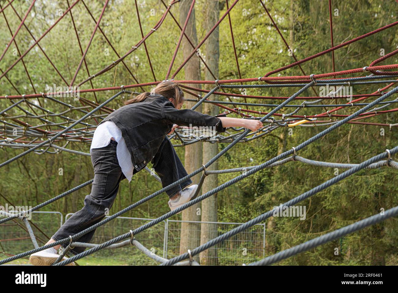 Teenage girl climbing on spider web with expression in public park ...