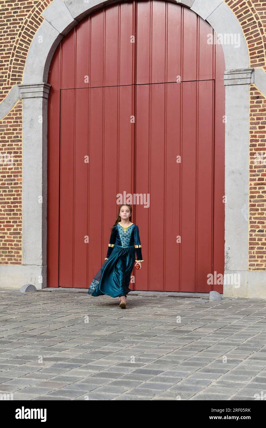 In a medieval dress, a girl holds an apple against the large red gate ...
