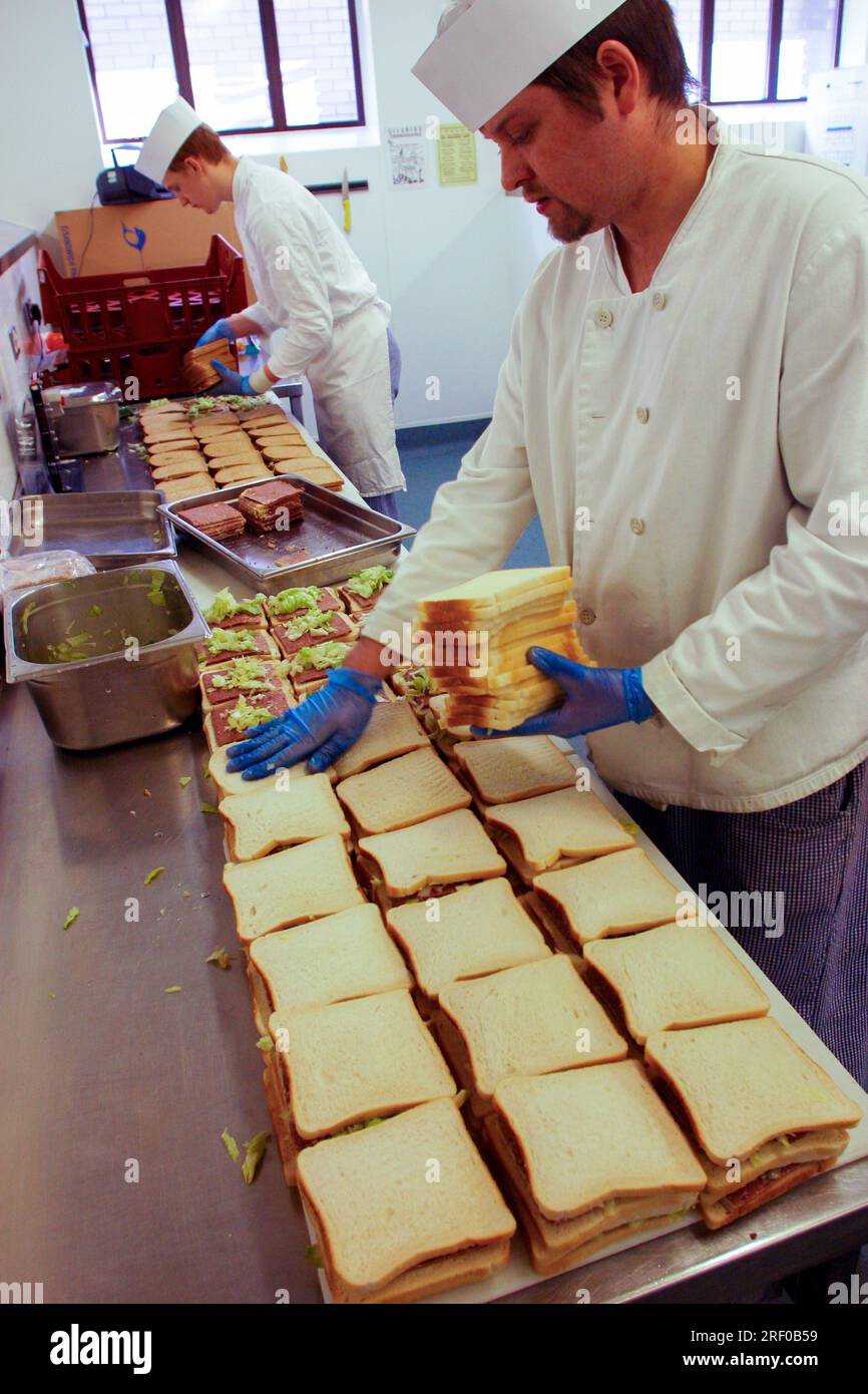 Cooks prepare multiple sandwiches in a hospital kitchen, adding lettuce ...