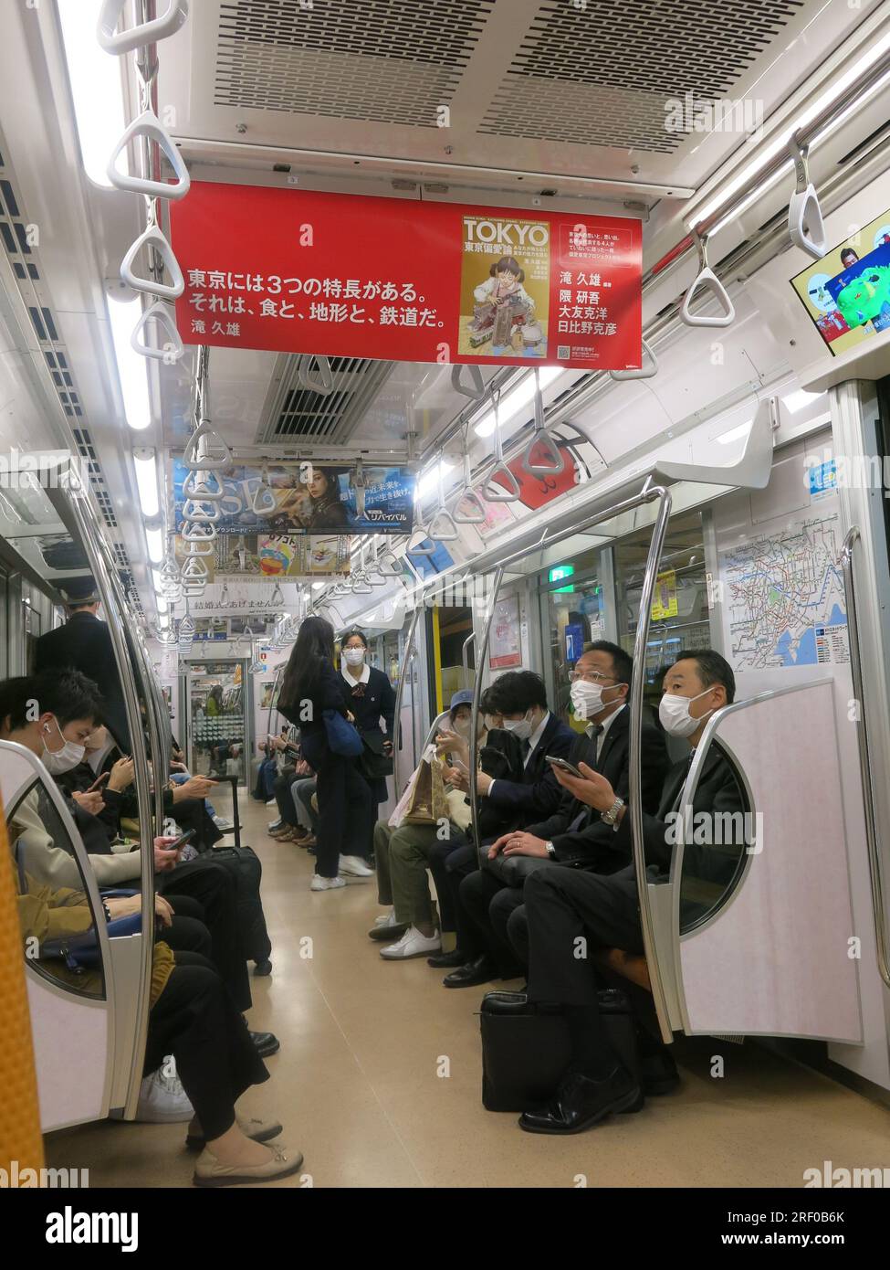 Japanese businessmen & commuters, some wearing facemasks, seated in a ...