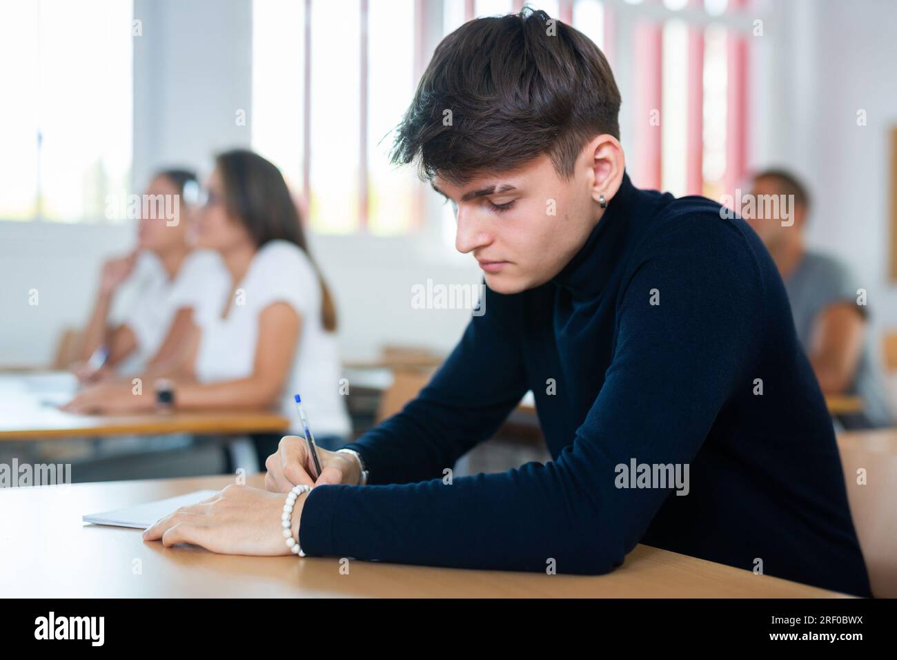 Focused guy listening and taking notes of lecture in university ...
