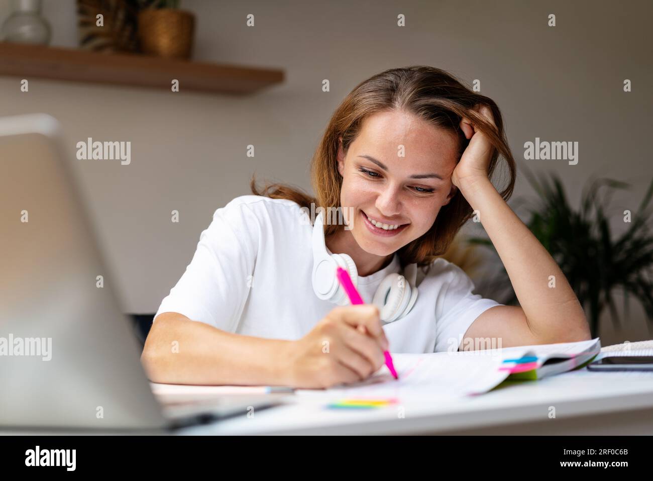 Young woman student doing homework, using pink marker pen for highlight ...