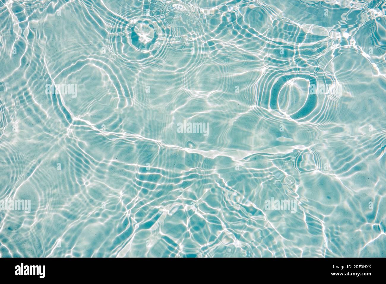 Turquoise water of a swimming pool shimmers in the summer sunshine ...