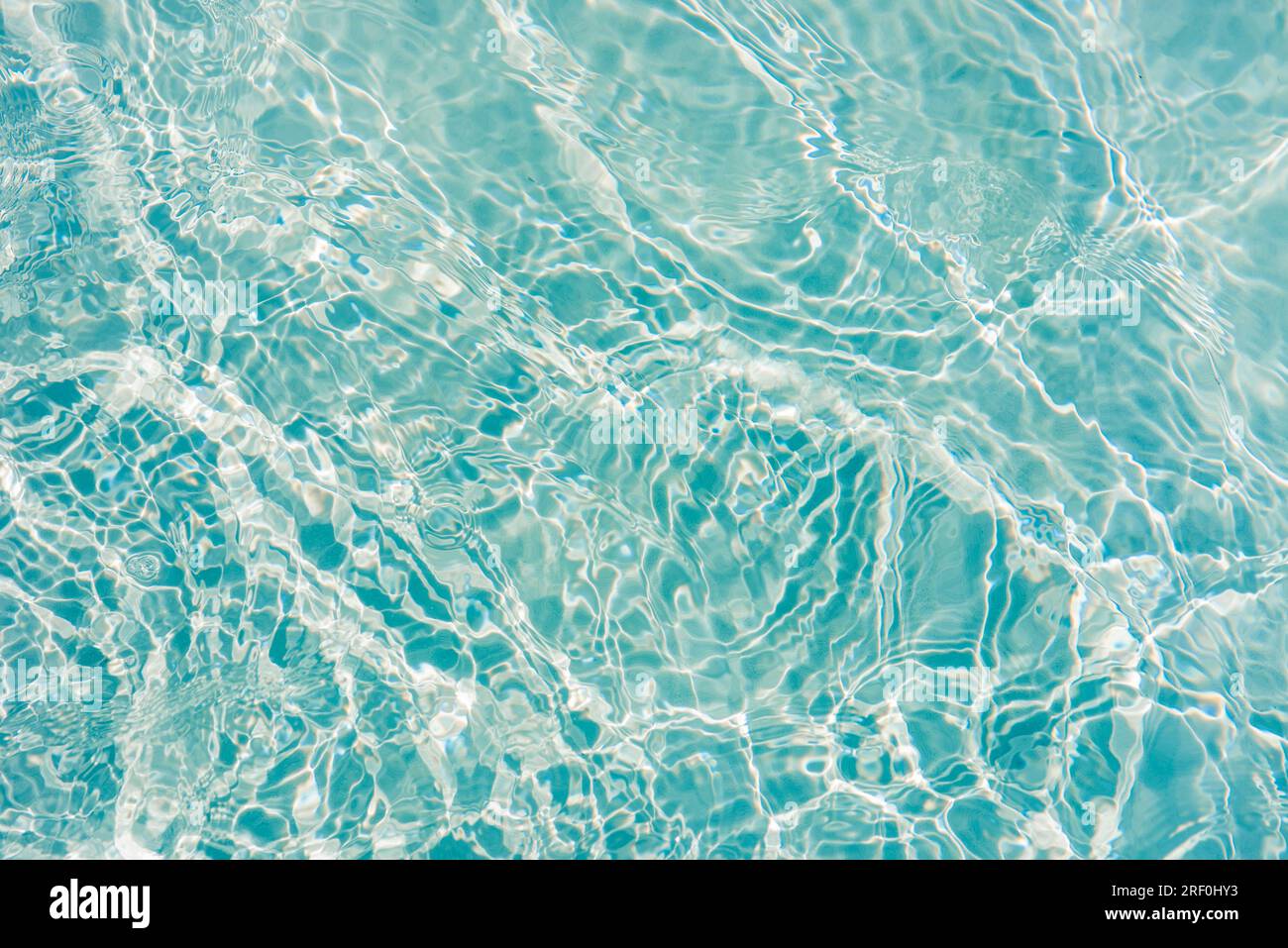 Turquoise water of a swimming pool shimmers in the summer sunshine ...