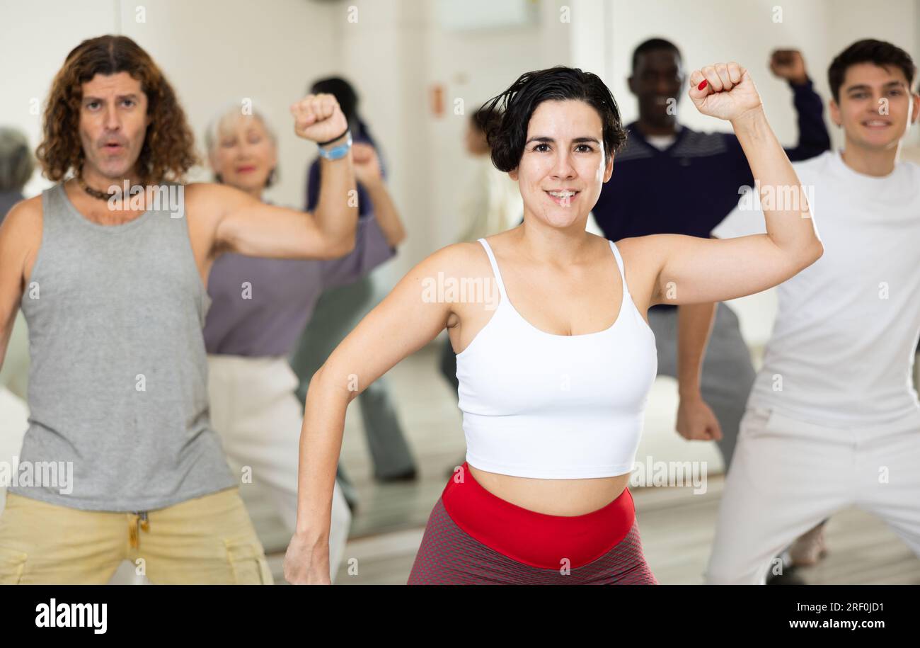 Happy young woman practising modern dance moves with other people in ...