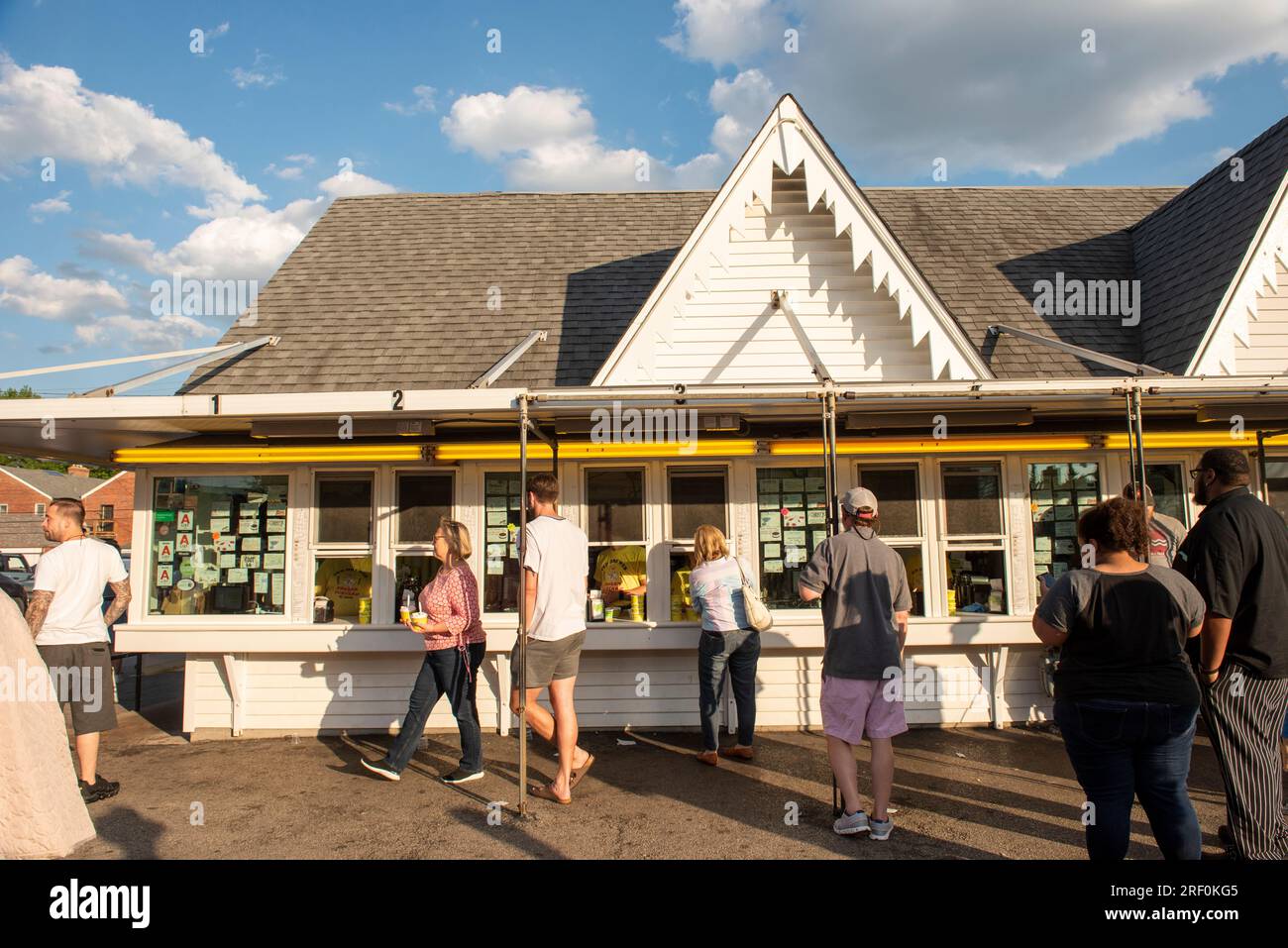 Dozens of people stand around in front of an ice cream shop waiting for ...
