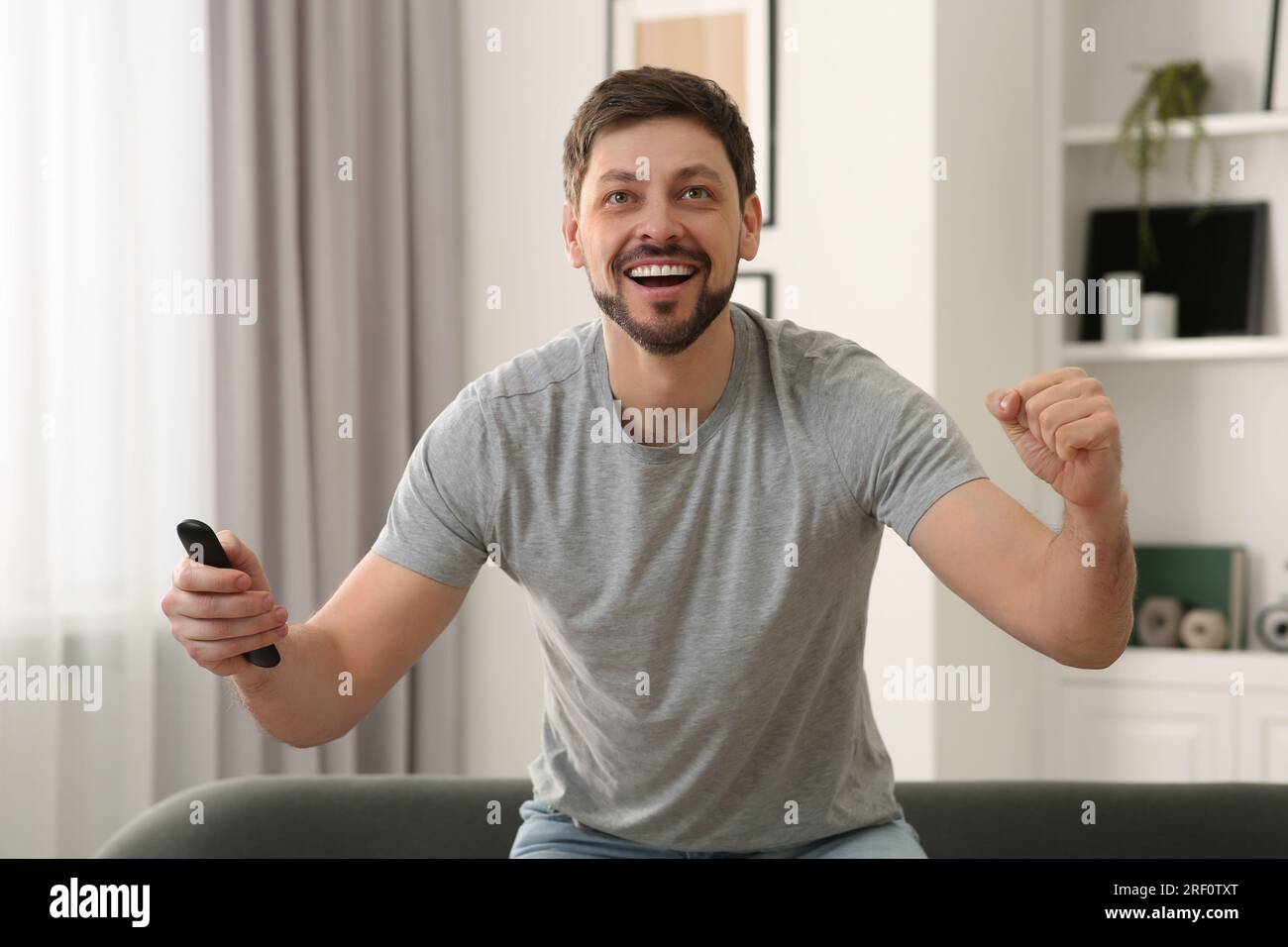 Emotional man holding remote controller and watching TV at home Stock ...