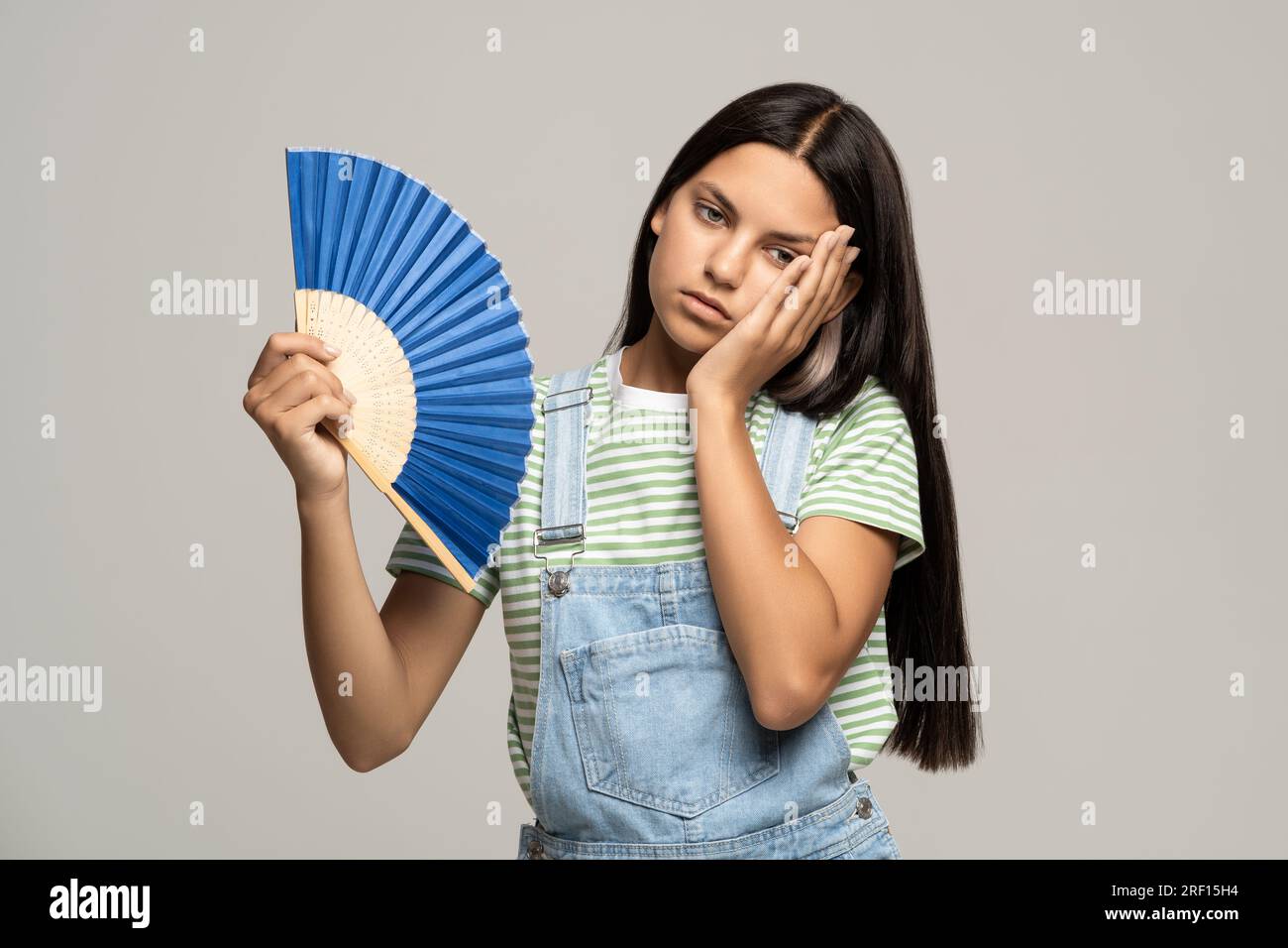 Sweaty teenage girl touching forehead using paper fan suffer from heat ...