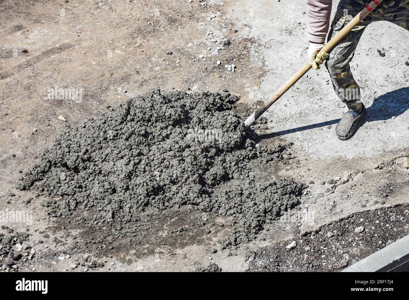 Road surface repair. Handyman with shovel scatters cement along road ...
