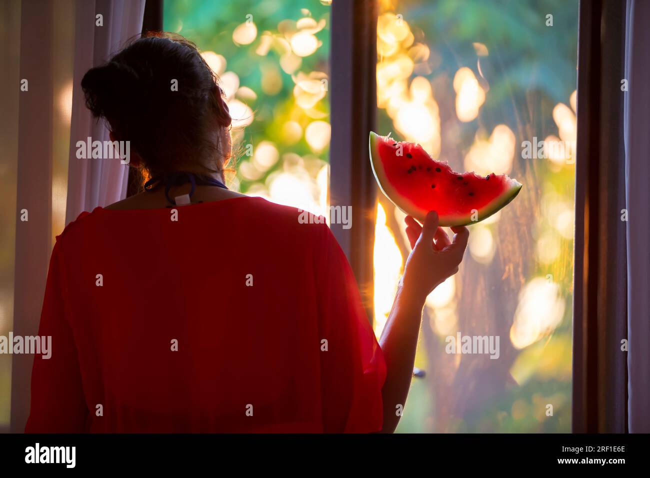 Silhouette of a woman at the window with a watermelon in the rays of ...