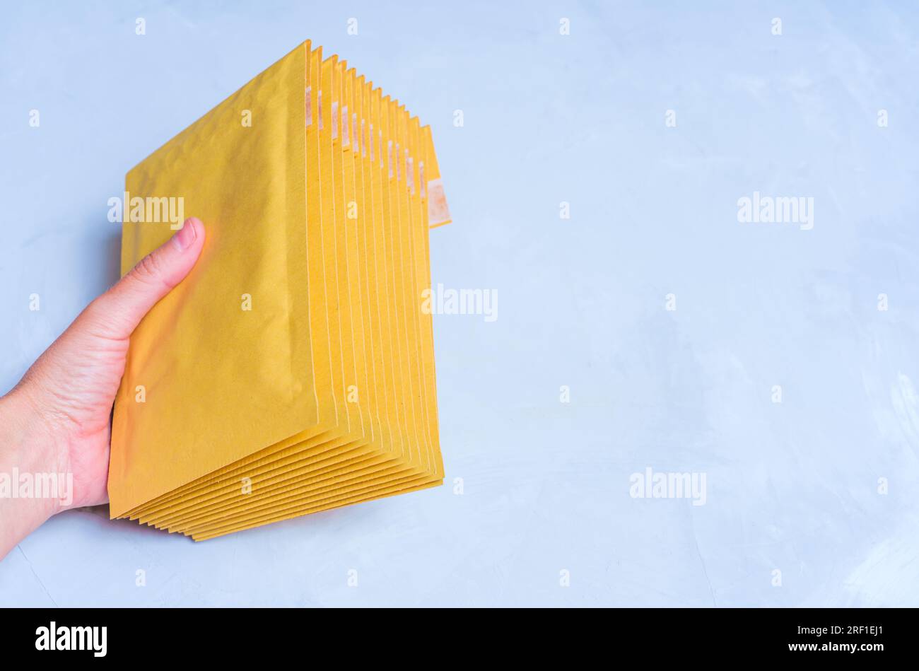 Hand holding a pile of yellow padded envelopes against a grey ...