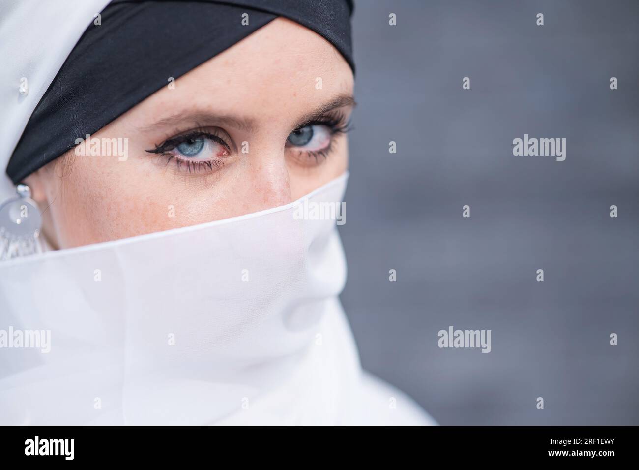 Portrait of a young blue-eyed woman in a hijab against a gray brick ...