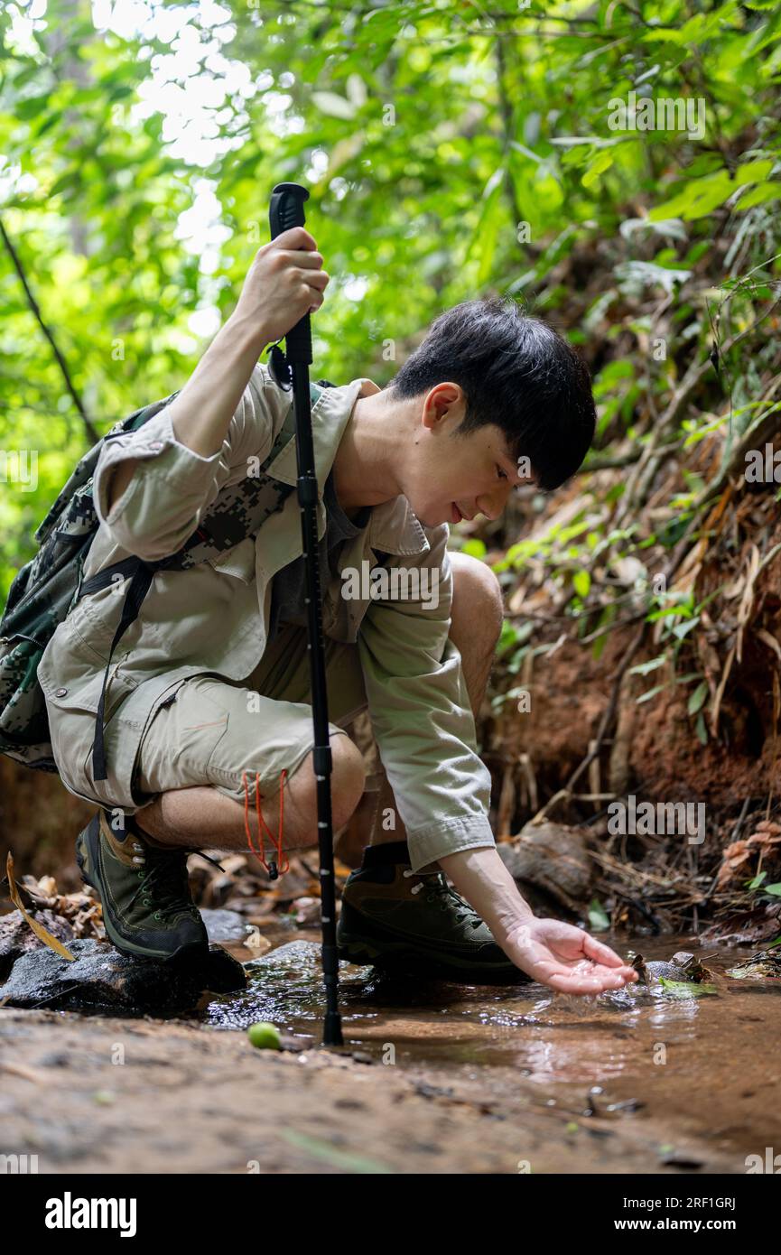 A portrait of an Asian male hiker sitting by the nature stream ...