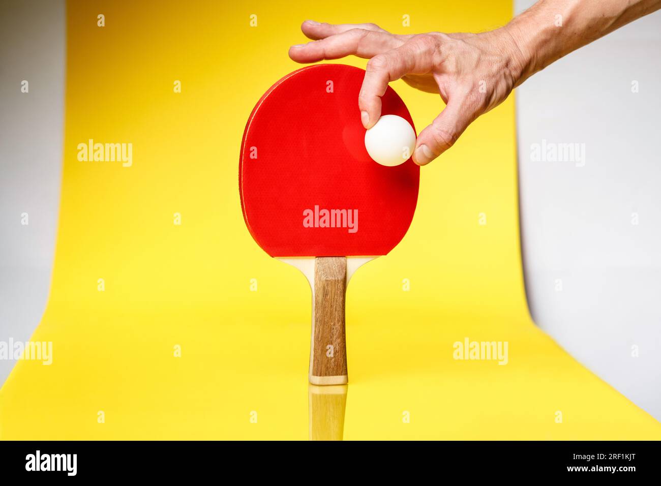 Male Hand Holding Ping Pong Ball Over The Red Side Of A Ping Pong