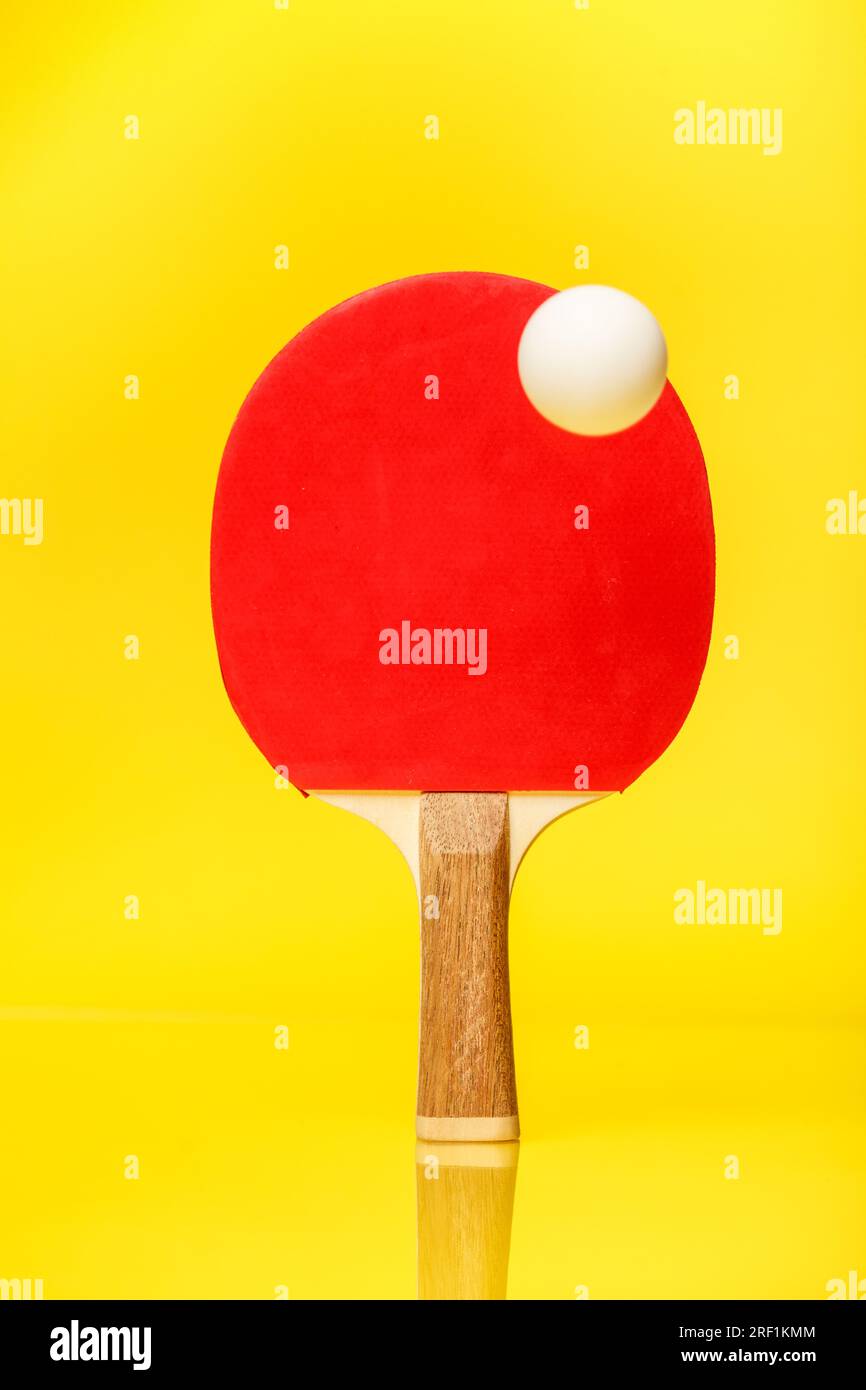 Red side of a ping pong racket with a white ball standing on a yellow ...