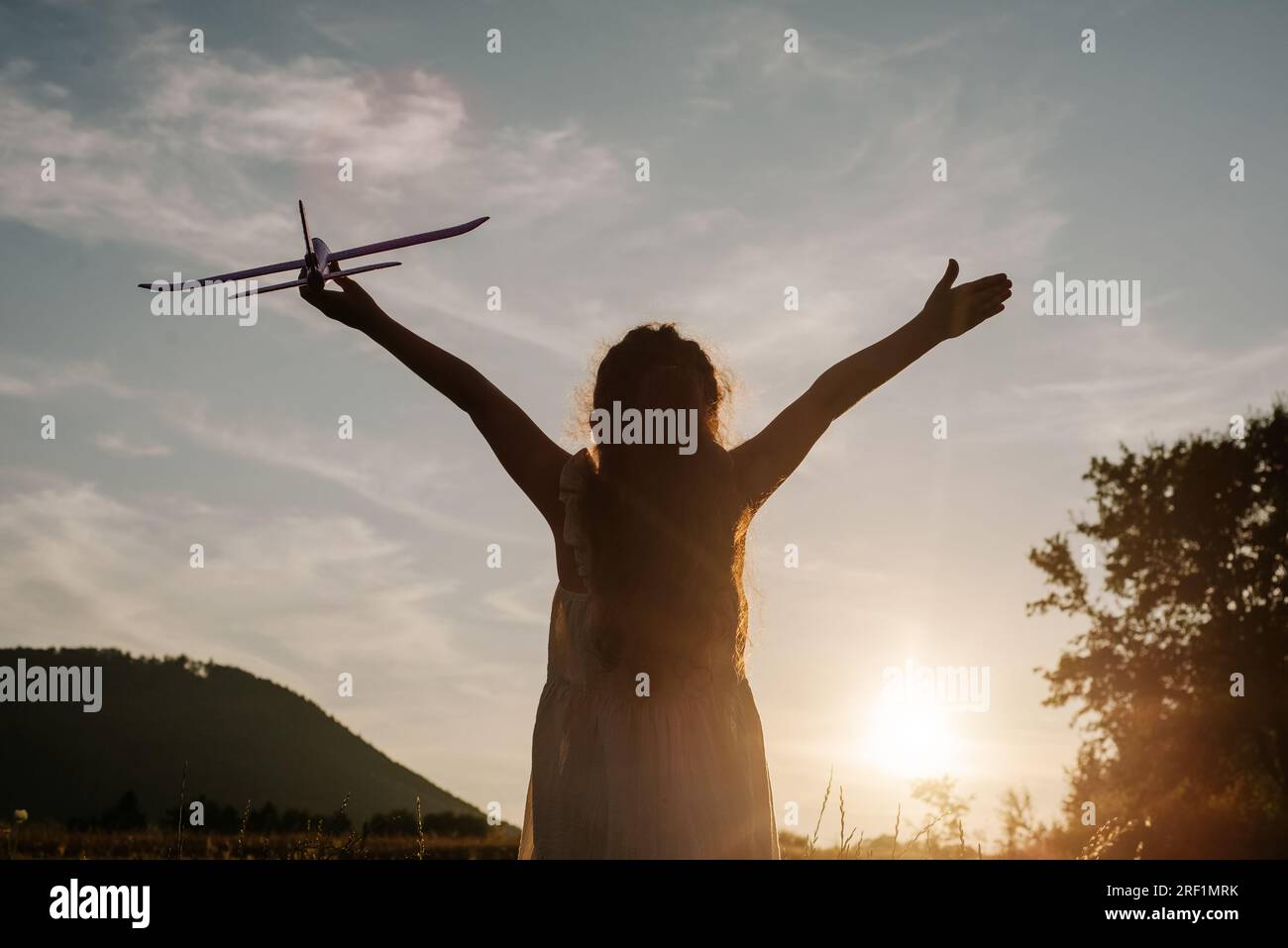 Cheerful preteen girl in dress holding violet toy airplane during ...