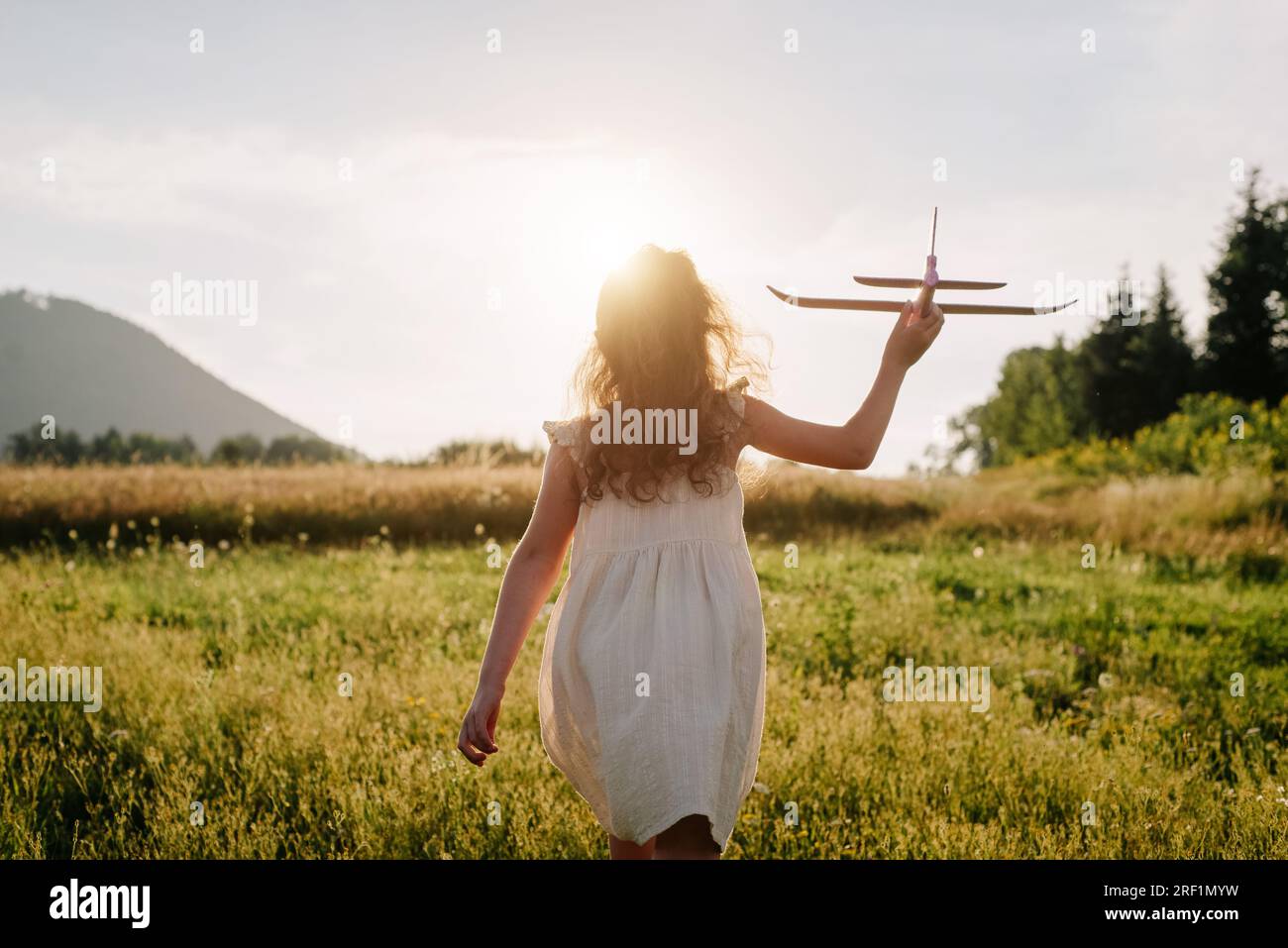 Back view of teen girl playing in dress with violet toy airplane during ...