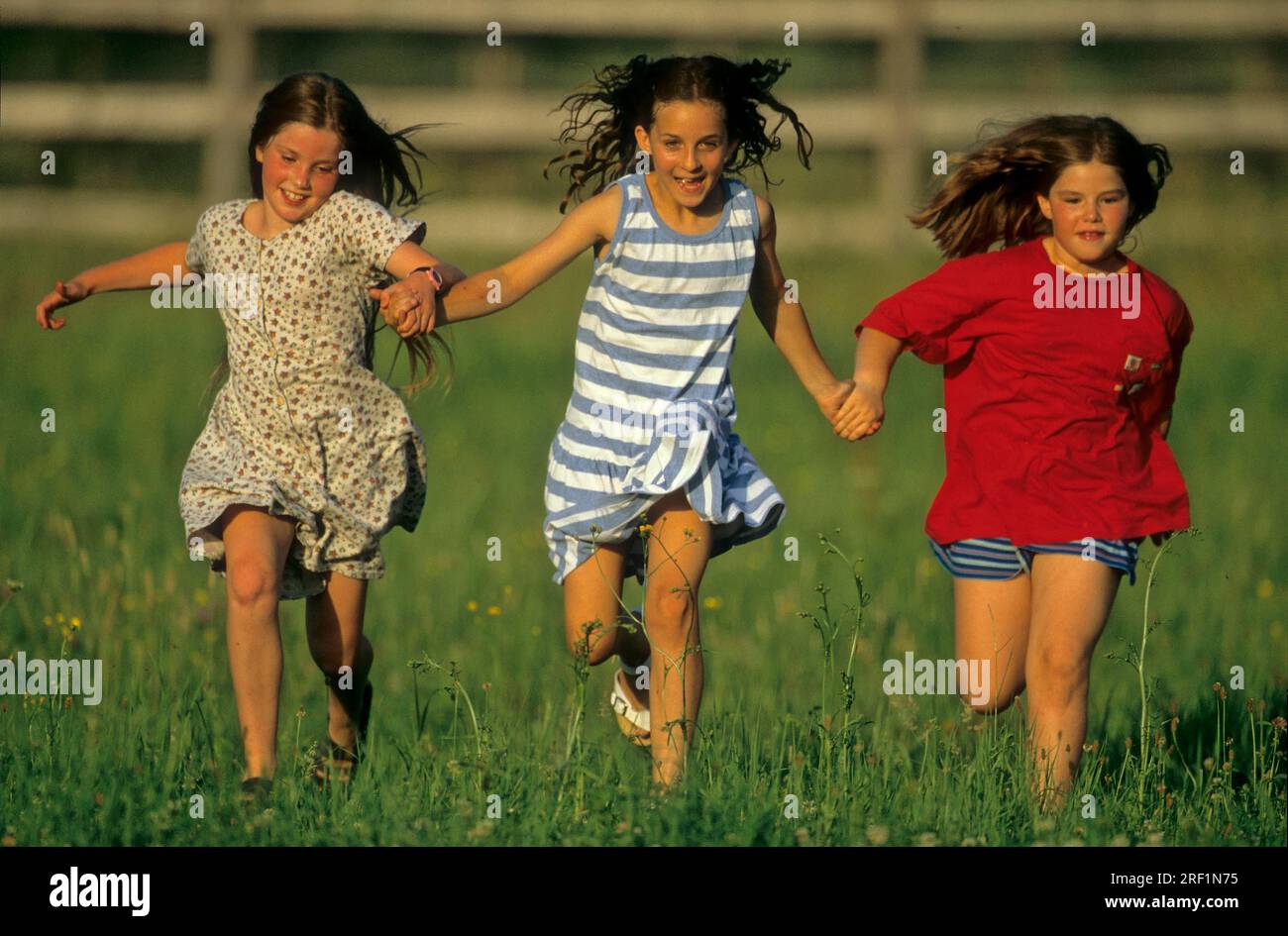 3 girls racing across green meadow Stock Photo - Alamy