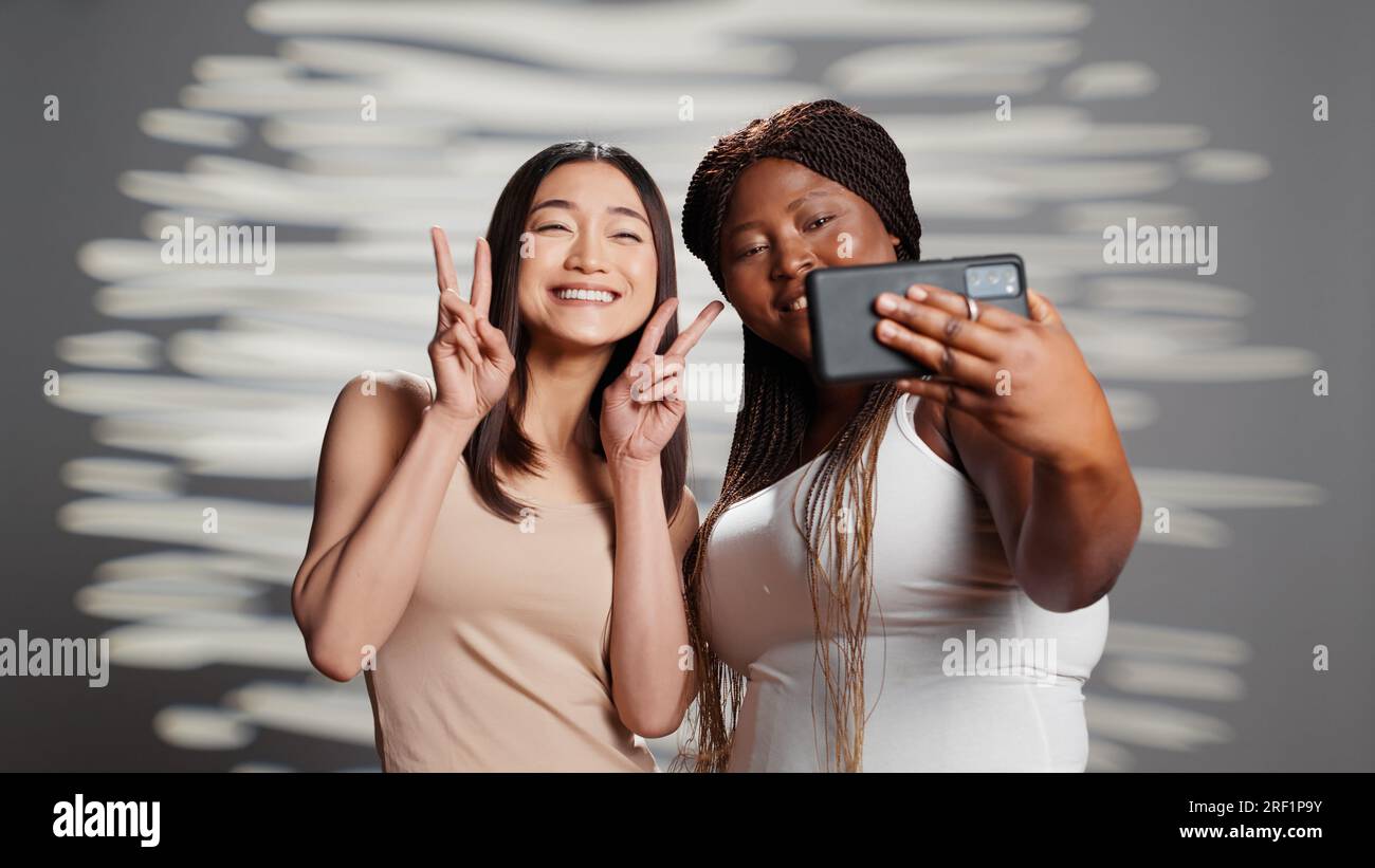 Happy flawless girls taking photos on mobile phone, using smartphone to ...