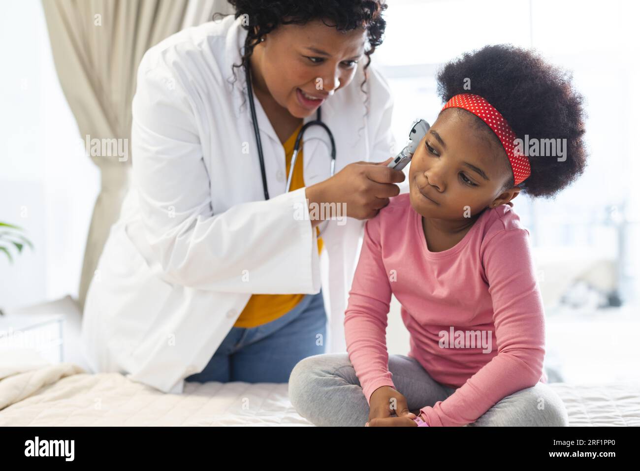 African american female doctor examining girl patient using otoscopy at ...