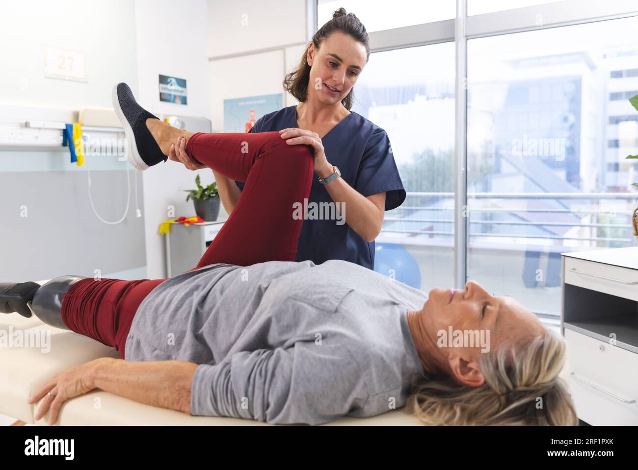 Caucasian female physiotherapist and senior woman with artificial leg stretching at hospital ...