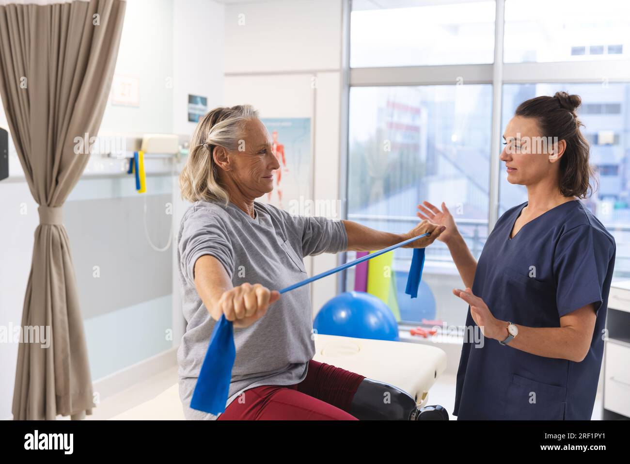 Caucasian female physiotherapist and senior woman with artificial leg using exercise band ...