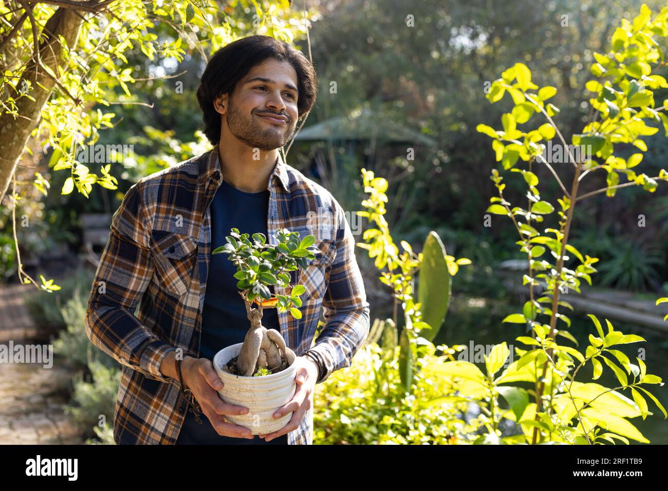 Happy indian man holding plant in sunny garden Stock Photo - Alamy