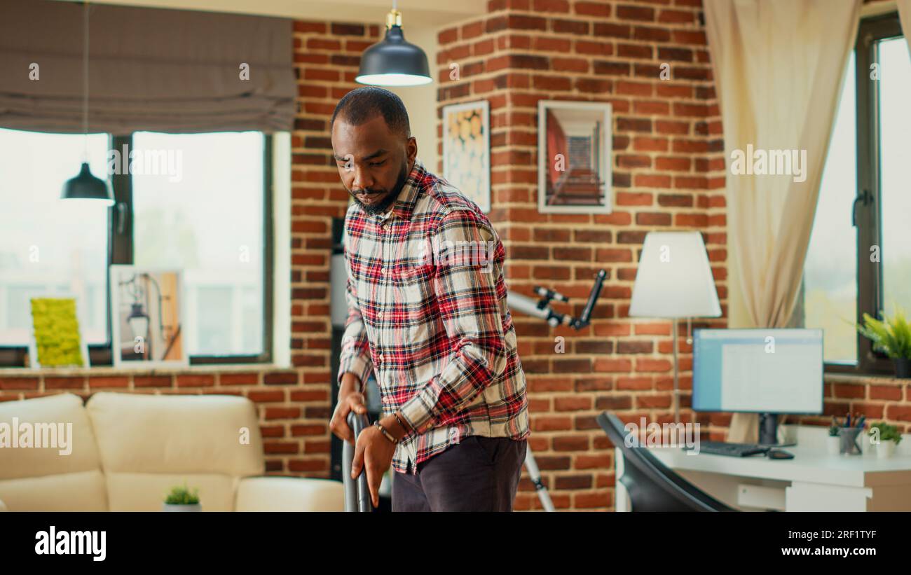 Modern male person doing spring cleaning session at home, using vacuum ...