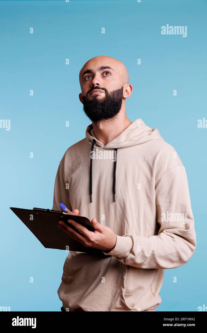 Pensive arab man holding clipboard and contemplating checklist while ...
