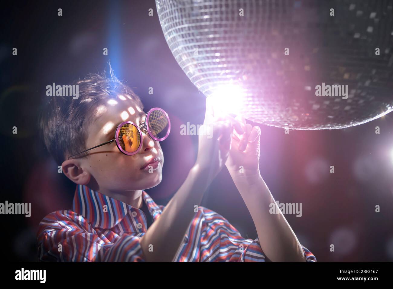 A young boy at an evening party in the rays of light and with a disco ...