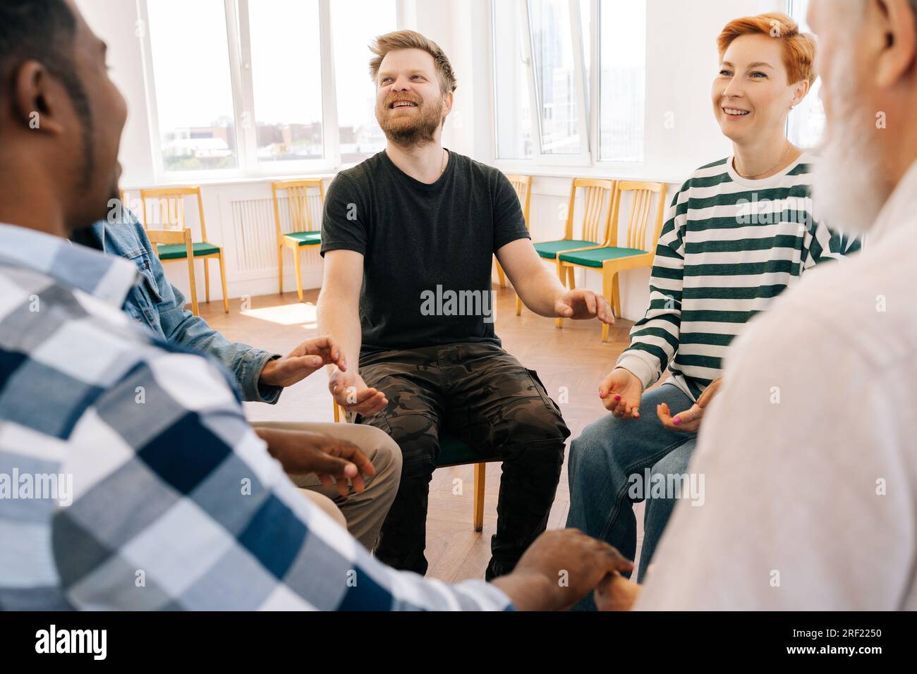 Group of happy multiracial people holding hands sitting in circle ...