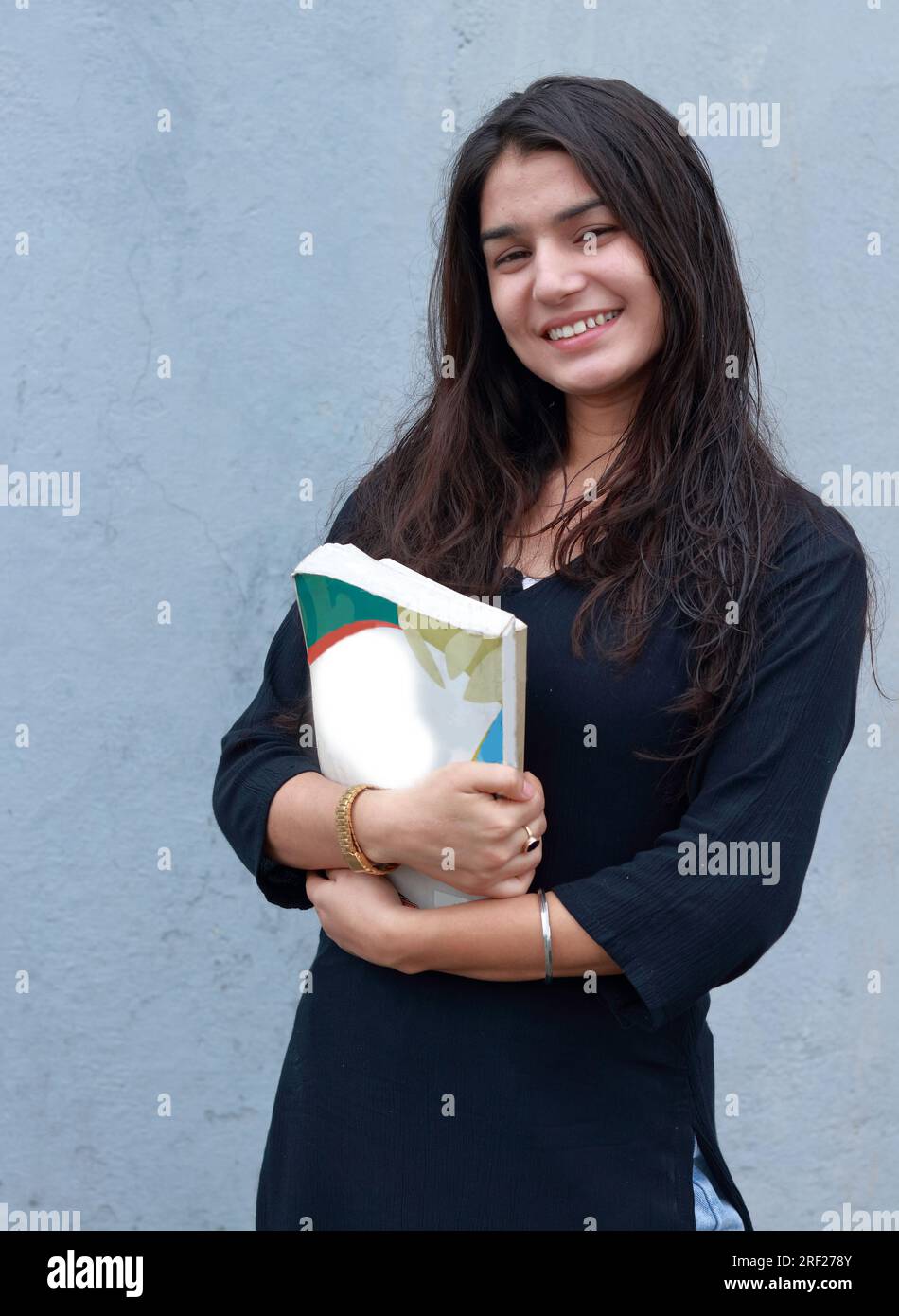 Photo of a beautiful Indian girl student holding a book and looking at ...