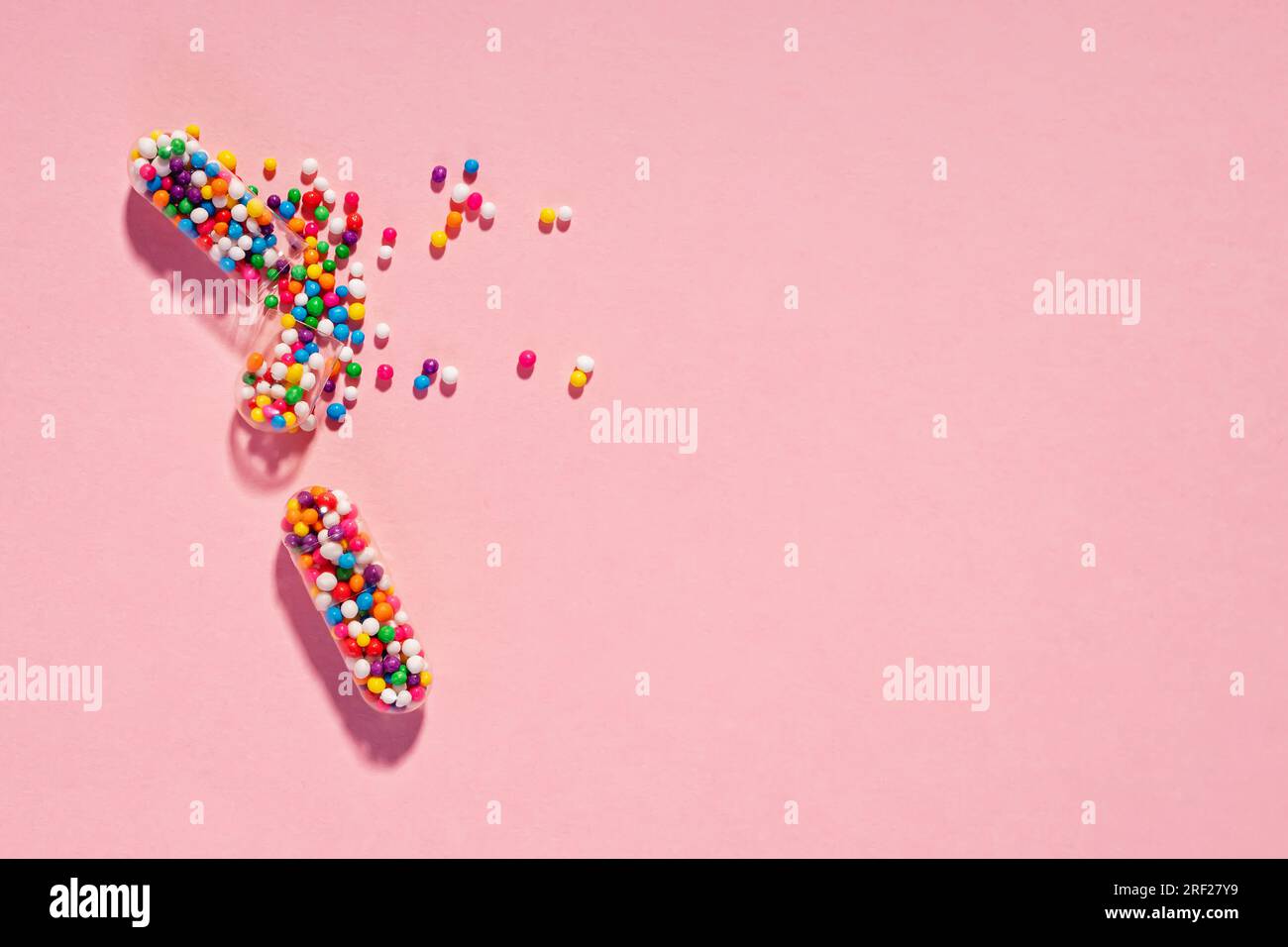 Medical pill capsules filled with colorful sugar sprinkles on pink ...