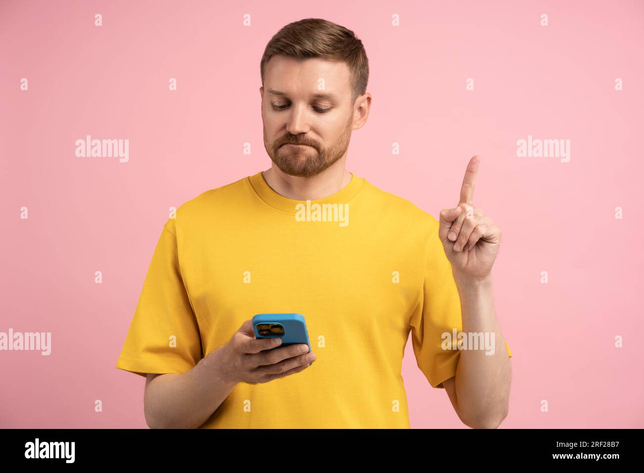 Sad upset man pointing index finger up looking in smartphone on pink ...