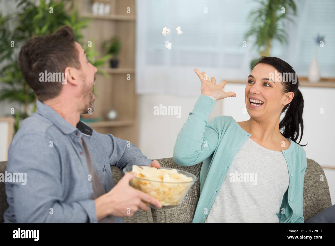playful girlfriend throwing popcorn in boyfriends mouth Stock Photo - Alamy