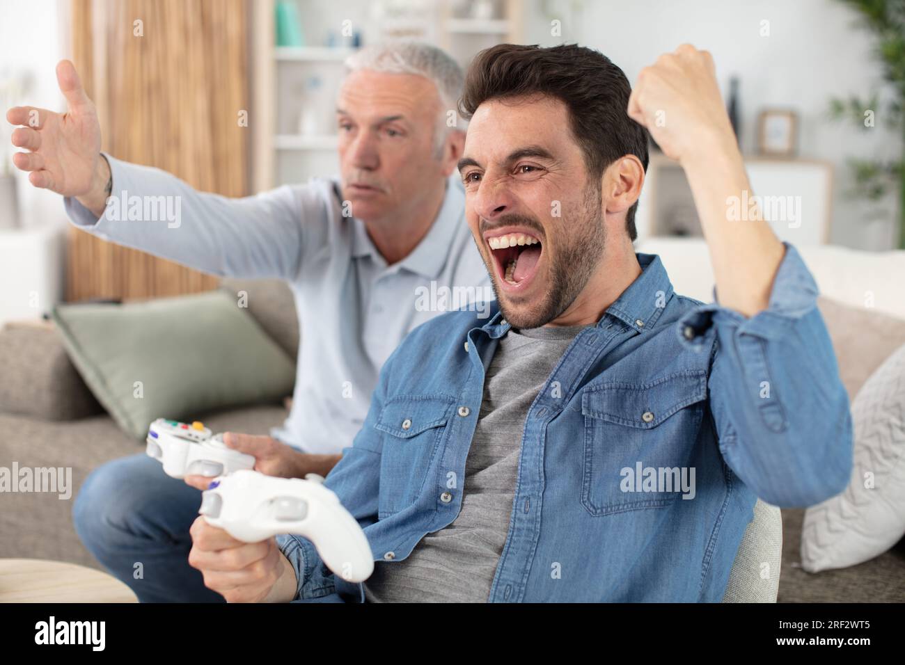 two guys playing on the console sitting on the couch Stock Photo - Alamy