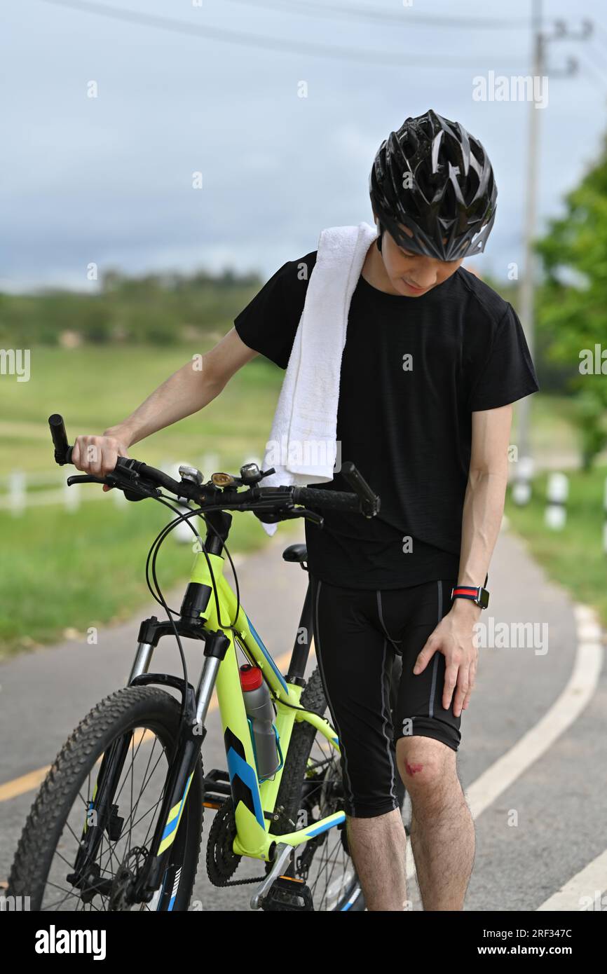 Asian male cyclist with injured knee carry bicycle walking in park ...