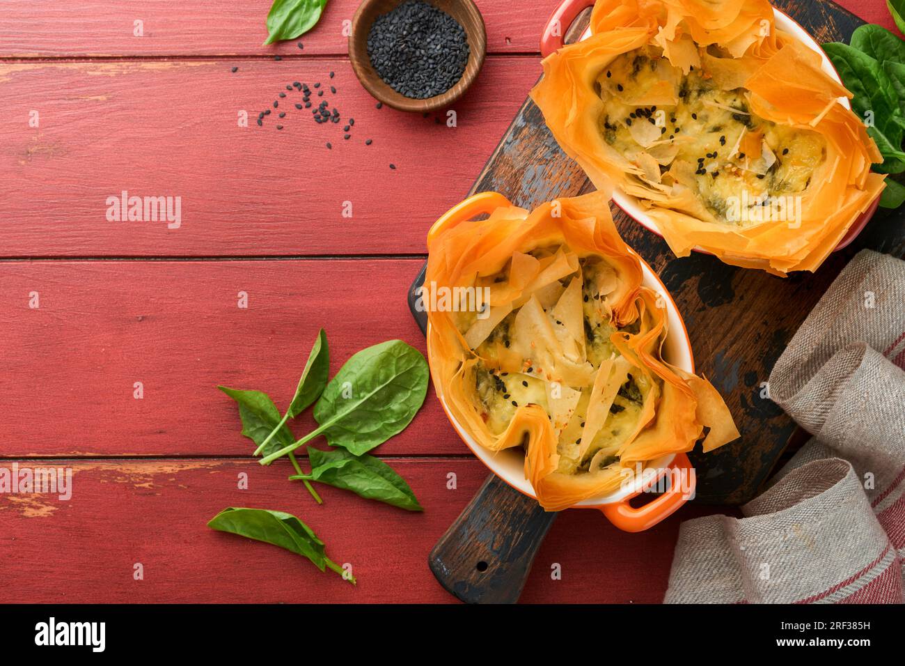 Filo pies with soft feta cheese and spinach in ceramic molds on old red ...